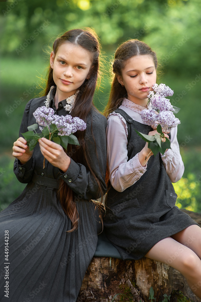 Two schoolgirls in school uniforms are sitting on the street with lilac ...