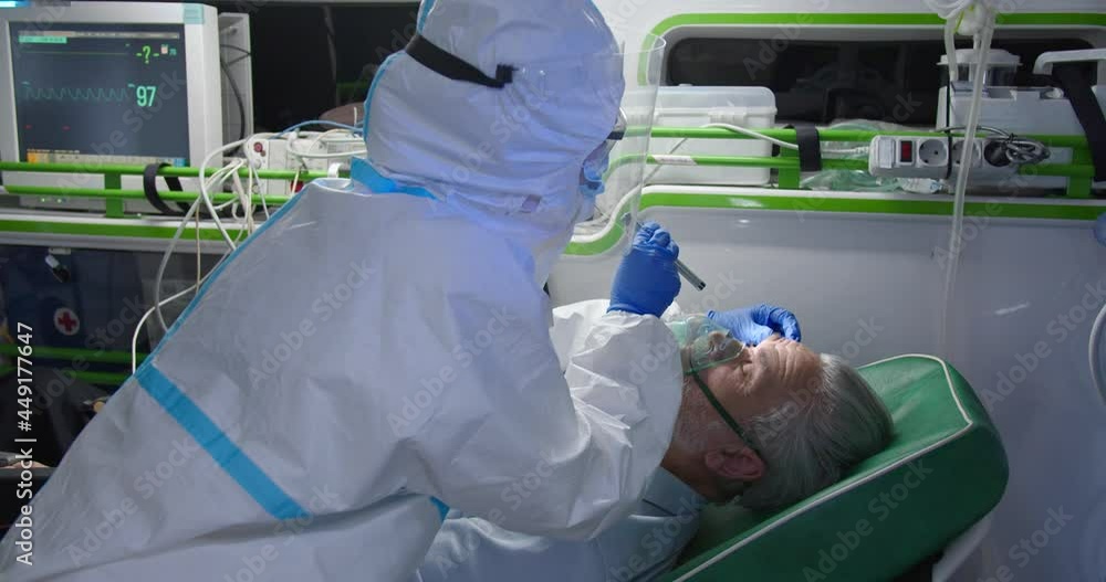 Medic in personal protective equipment saving life of old man in ambulance. Medic giving oxygen ...