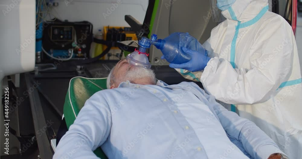 Medic in personal protective equipment bringing old man in oxygen mask ...