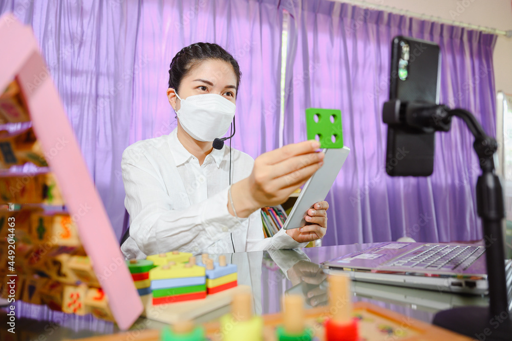 Asian female teacher wearing a mask is teaching students to study ...