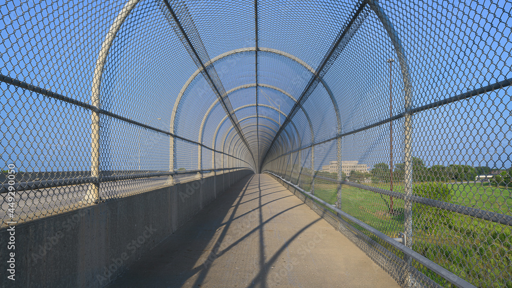 Pedestrian highway overpass enclosed by cyclone fencing under clear ...