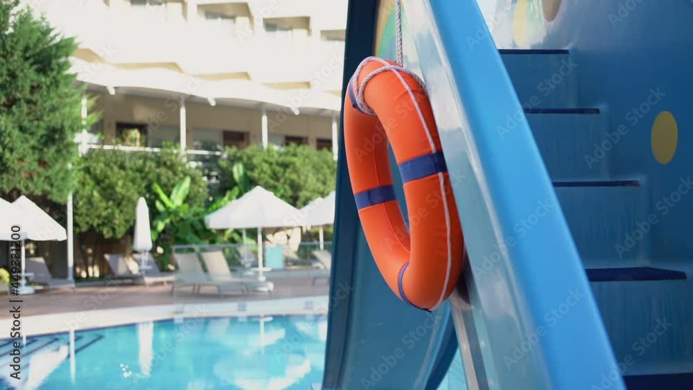Red blue lifebuoy hangs on large plastic slide stairs by hotel swimming ...