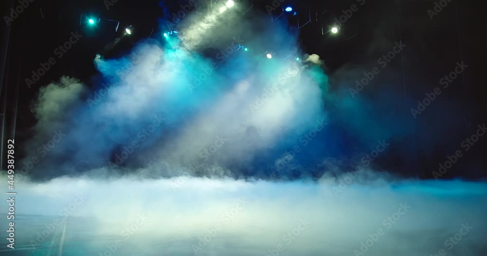 Rotating beams of stage light shine through the heavy white smoke, they ...