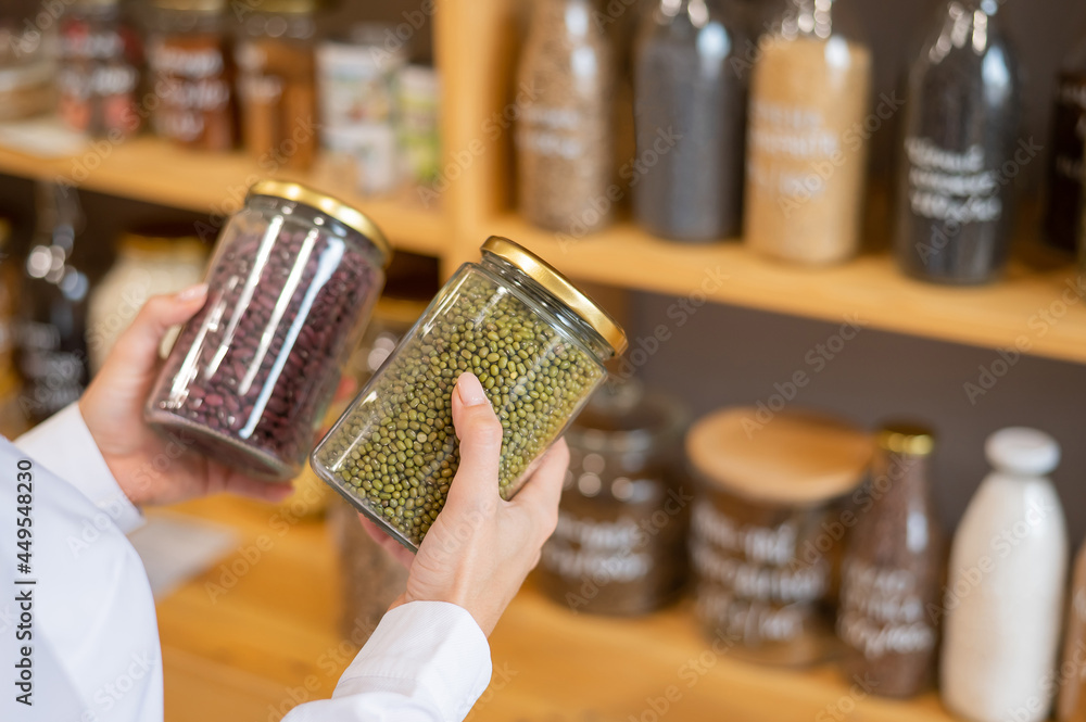 A woman holds glass jars of cereals in an eco friendly store. The ...