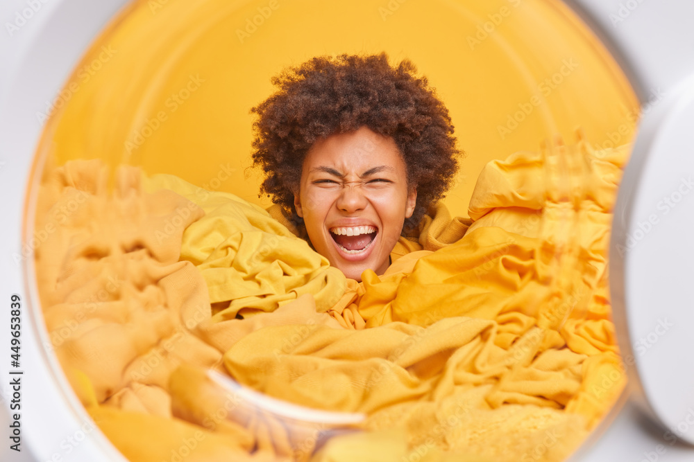 Emotional curly haired housewife poses inside of washing machine buried ...