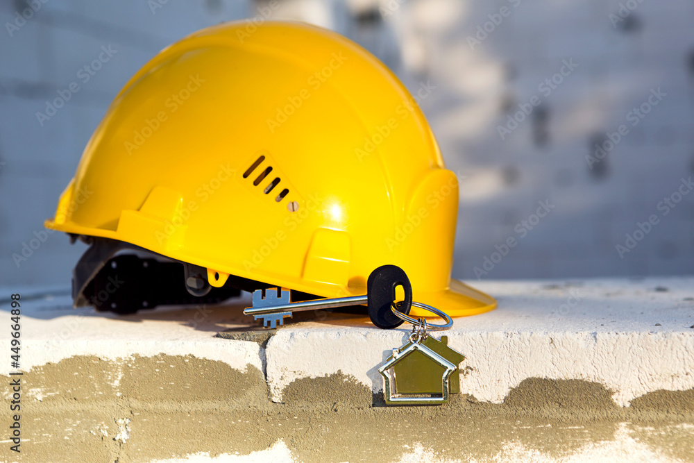 Construction yellow hardhat and key to house on window of housing made ...