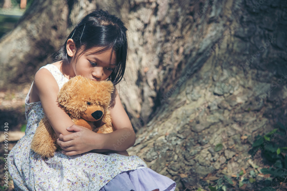 Sad girl hugging teddy bear sitting under tree sadness alone in green ...