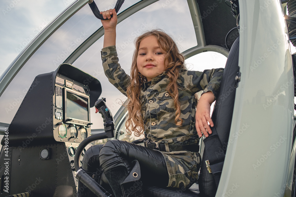 Smiling tween girl in camouflage dress sitting in helicopter cockpit ...