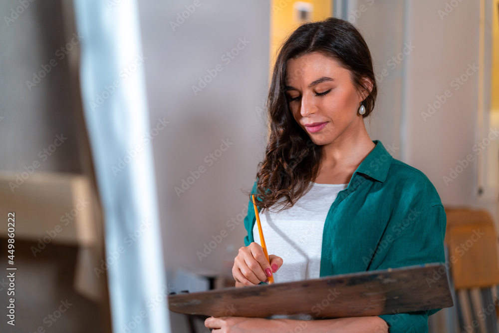 painting teacher with green eyes drawing on canvas with smile and using ...