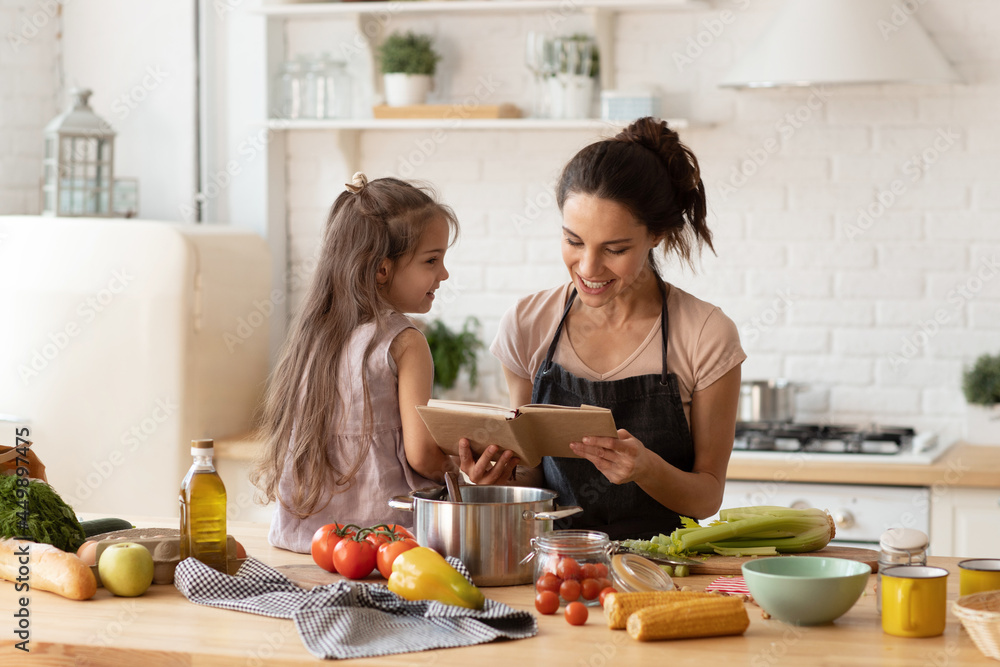 Beautiful young mother reading to adorable daughter on kitchen. Mom and ...