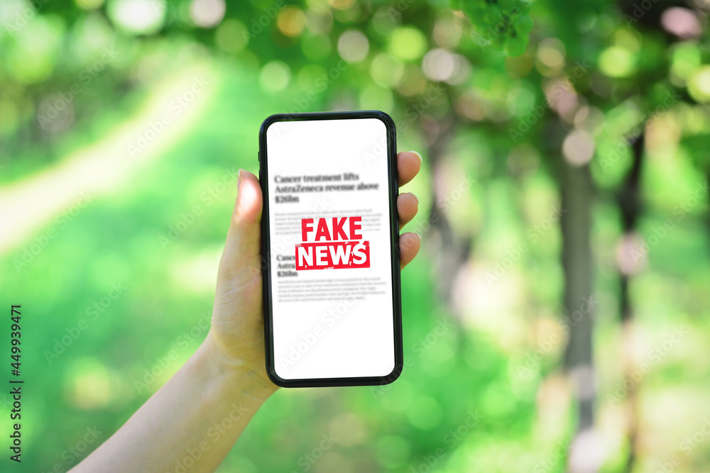 Online fake news on a mobile phone. Holding a smartphone with fake news ...