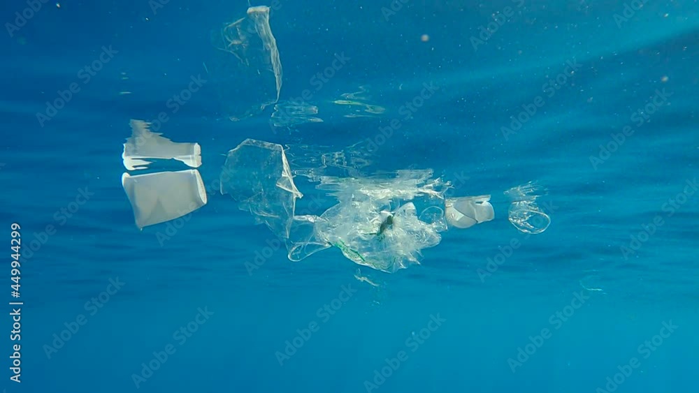 A lot of plastic trash floats by water reflecting from its surface ...