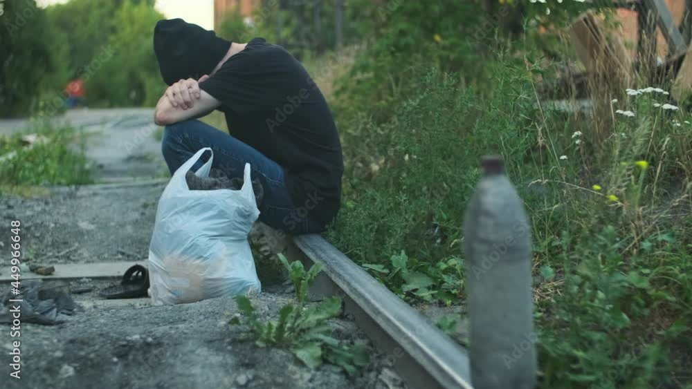 Homeless man with his belongings sleeping, siting on the railway ...
