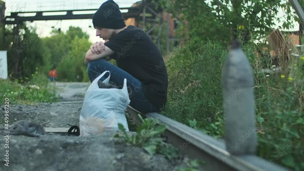 Homeless man with his belongings sleeping, siting on the railway ...