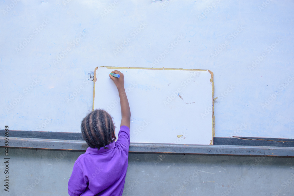 African girl child, pupil or student sitting down and writing in a ...