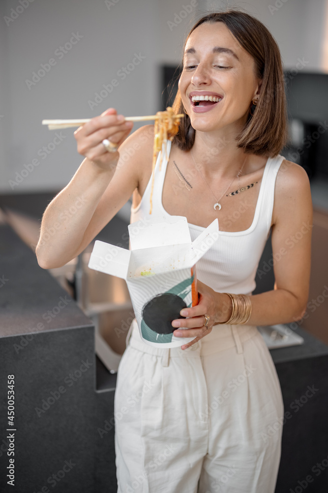 Young woman eating noodles with chopsticks from cardboard packaging in ...