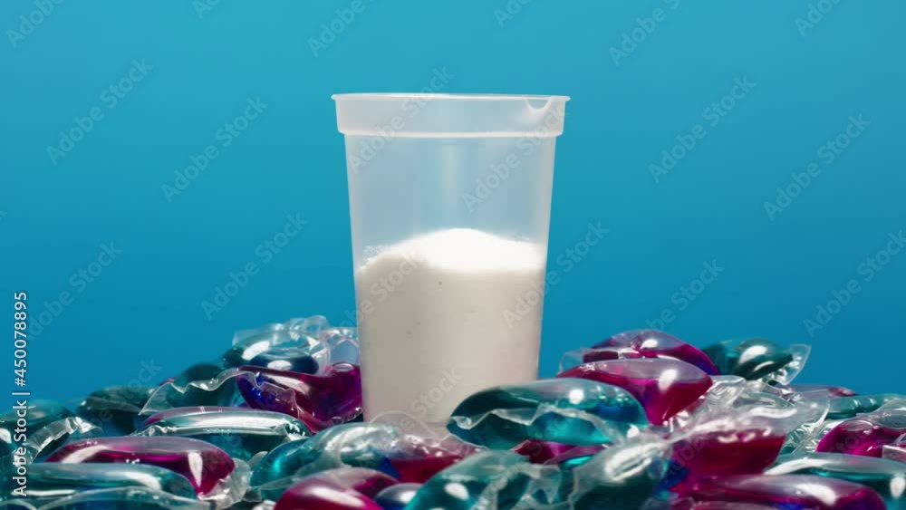 Washing gel pods and plastic glass with detergent powder on blue ...