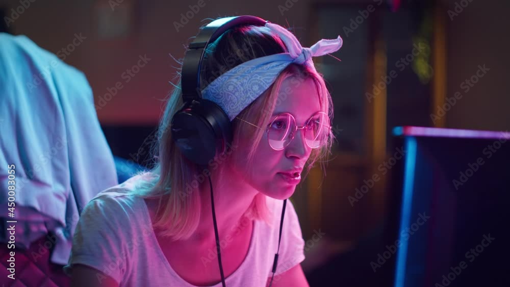 Young woman wearing headphones playing computer game at night. Female ...