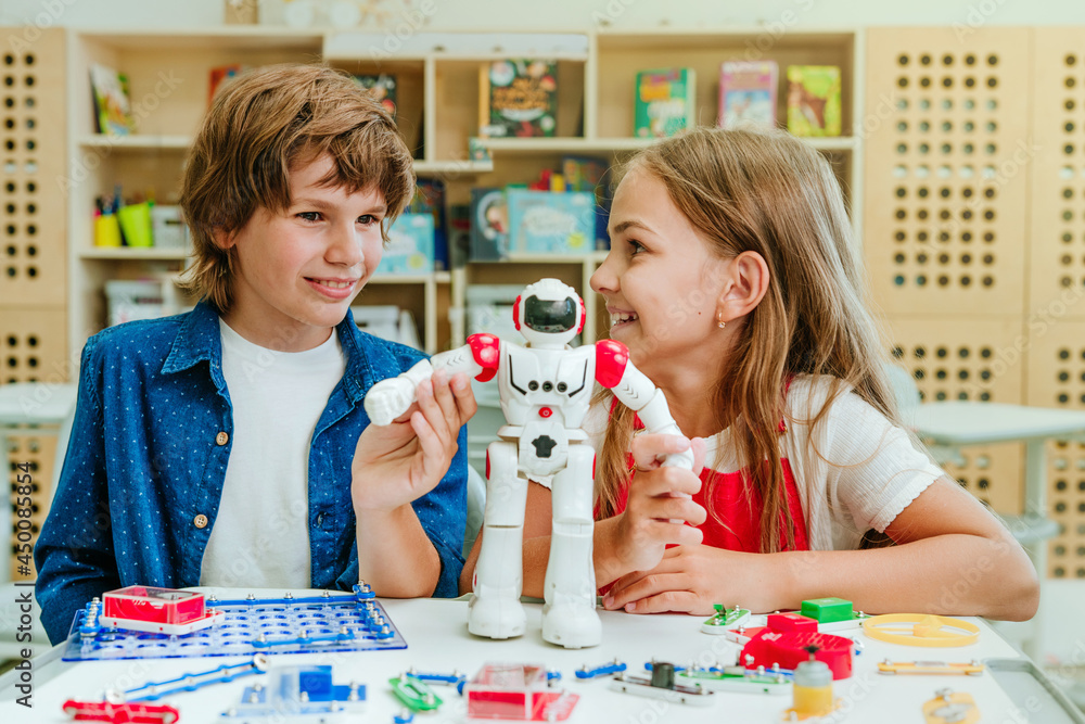 Teenage boy and girl play with robot during a lesson in the classroom ...