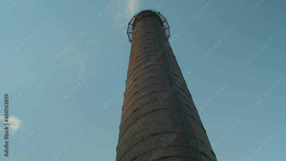 Huge brick pipe stretching into the light blue sky with rare clouds ...