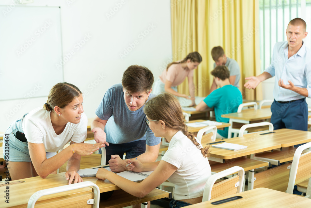 Pupils sitting in class by groups and performing task. Teacher standing ...
