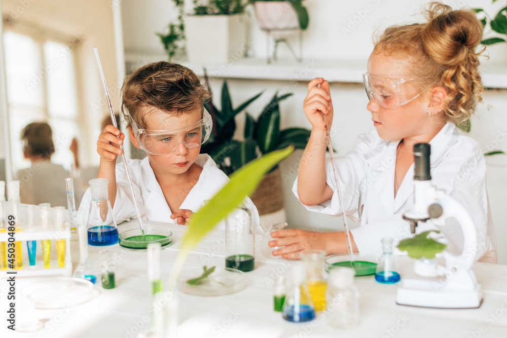 Serious little boy and girl in white uniforms conducting chemical ...