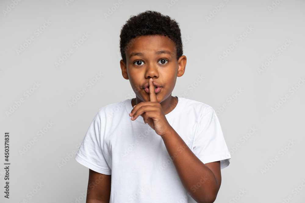 Shh, be quiet. Portrait of funny cute little boy with curly hair in T-shirt making silence ...