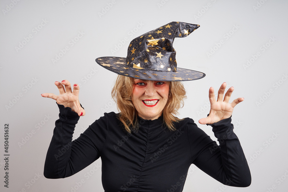 witch in a black hat makes a frightening gesture with her hands ...