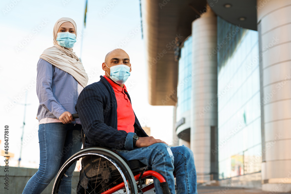 Muslim woman and disabled man in wheelchair smiling and looking at ...