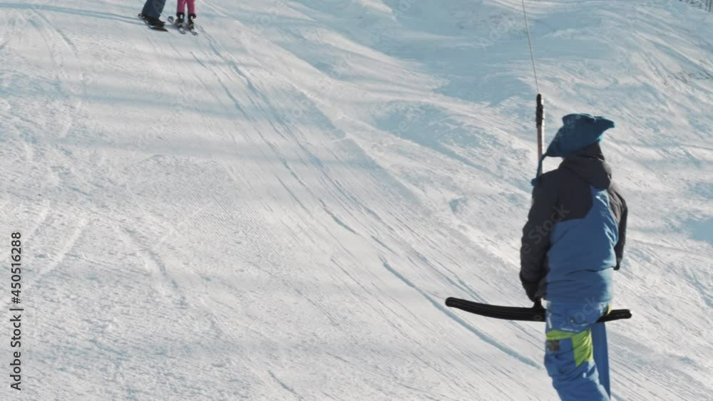 A snowboarder using a T-bar lift to climb a hill or a mountain on a ...