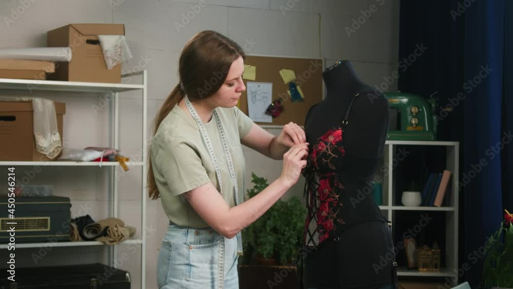 Dressmaker taking fitting corset on mannequin and typing on gadget ...