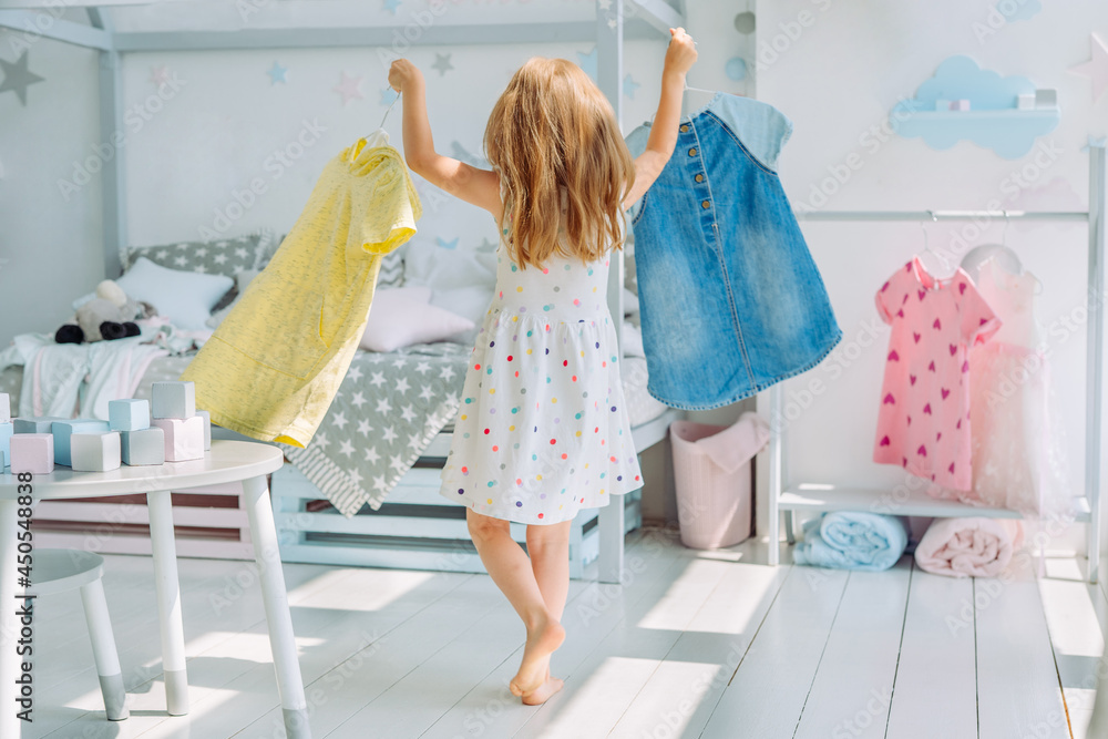 Beautiful little girl choosing a dress in the kids room Stock Photo ...