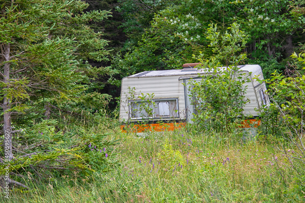 An abandoned travel trailer, white and orange in color, deserted in a ...