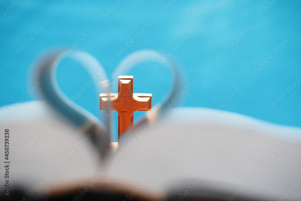 Wood crucifix in light, behind blurred heart shape bible page on blue ...