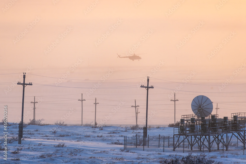 Industrial arctic landscape. A helicopter is landing at an airstrip in ...