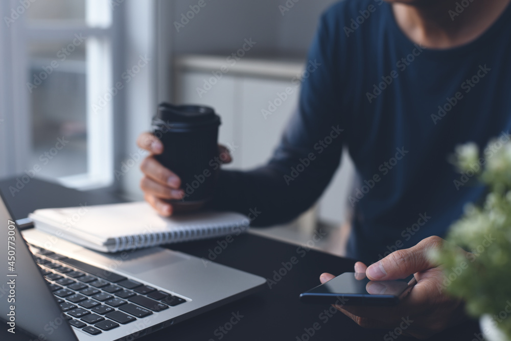 Casual man using smartphone, working on laptop computer from home ...