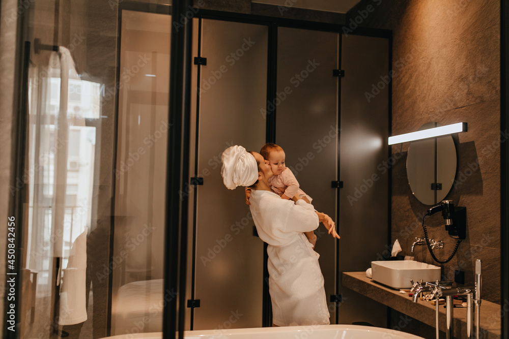 Slender woman in clothes after shower tightly hugs her beloved child ...