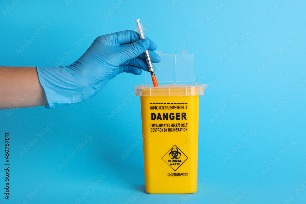 Doctor throwing used syringe into sharps container on light blue ...
