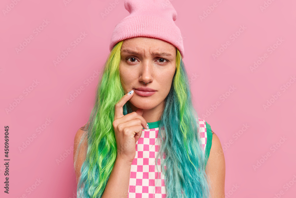 Young sad female model with long dyed hair keeps finger near corner of ...