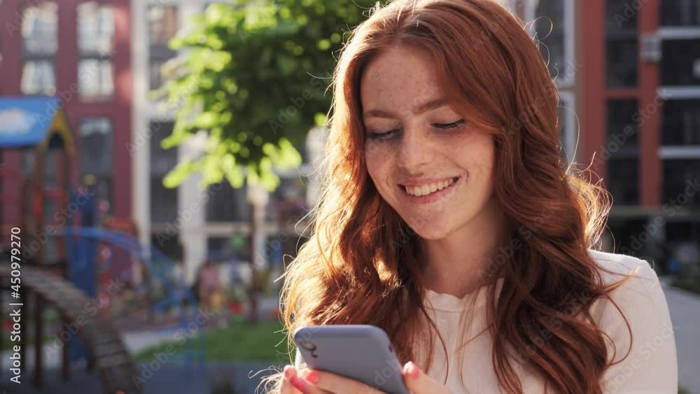 Positive charming young ginger lady using mobile phone for browsing ...