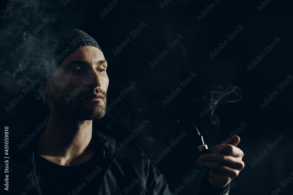 Man smokes smoking pipe against dark background. Back side lit profile ...