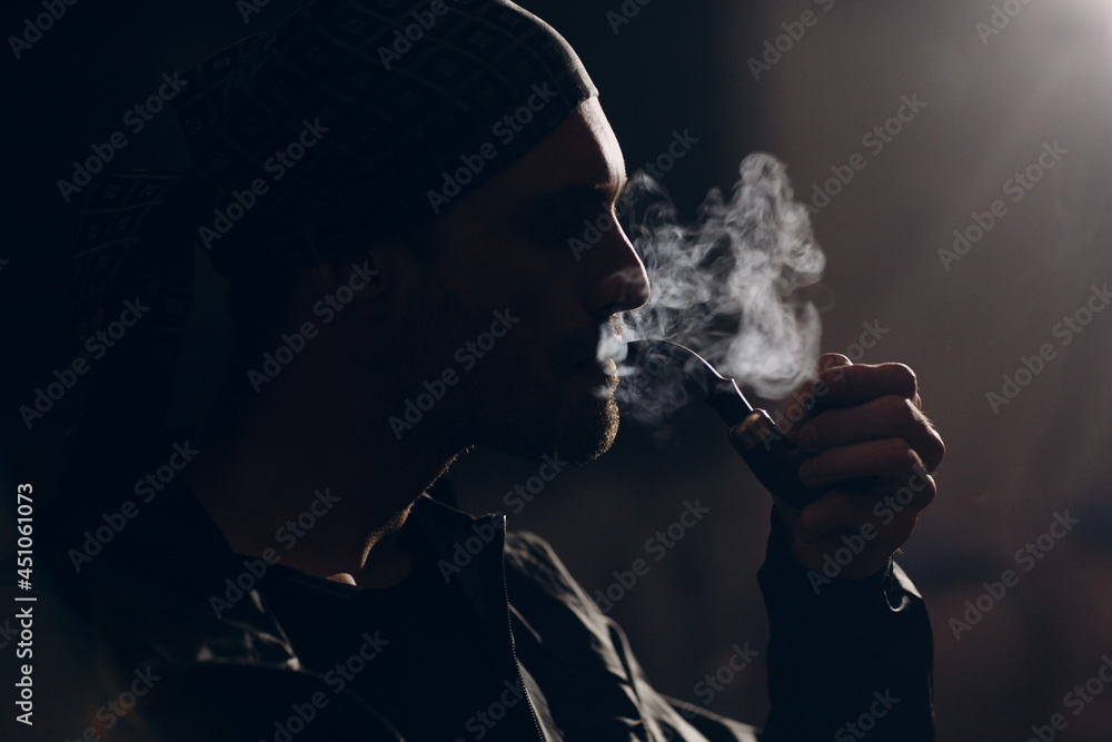 Man smokes smoking pipe against dark background. Back side lit profile ...