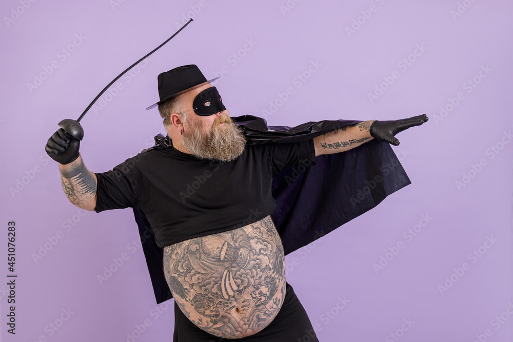 Mature bearded fat man in Zorro costume with large bare abdomen stands ...