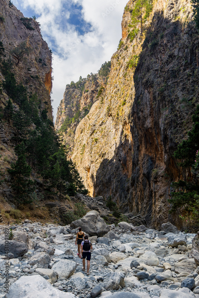 Hikers in a huge natural gorge with towering cliffs and pine trees ...