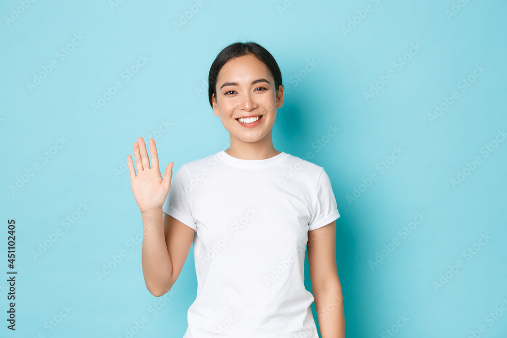 Portrait of friendly cheerful asian girl in white t-shirt saying hello ...