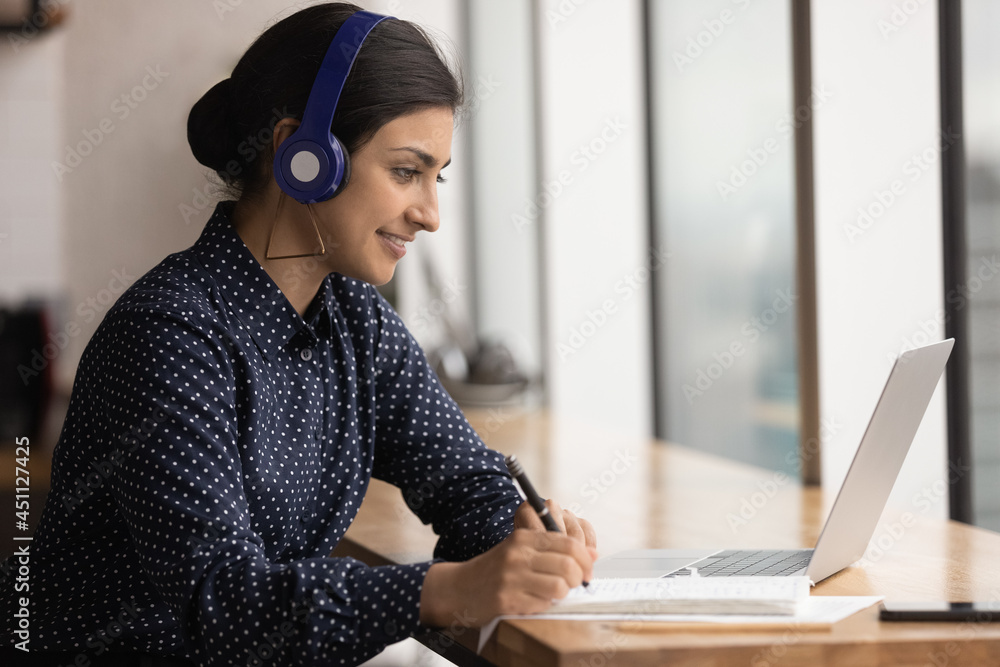 Attractive young Indian woman sit table wear headphones listen to audio ...