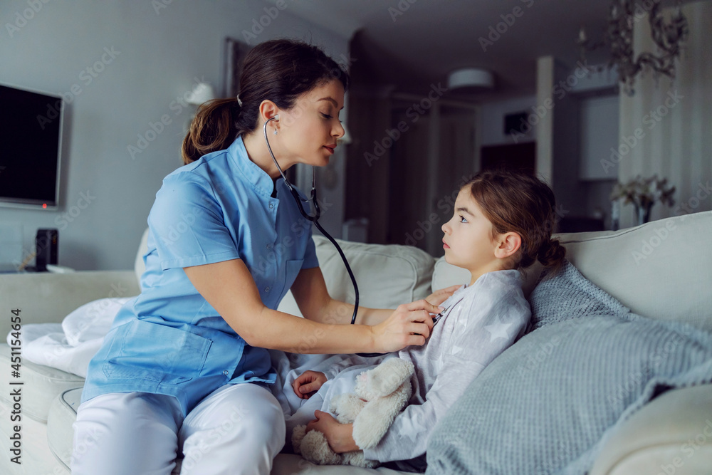 Doctor sitting on sofa next to girl and examining her lungs with ...