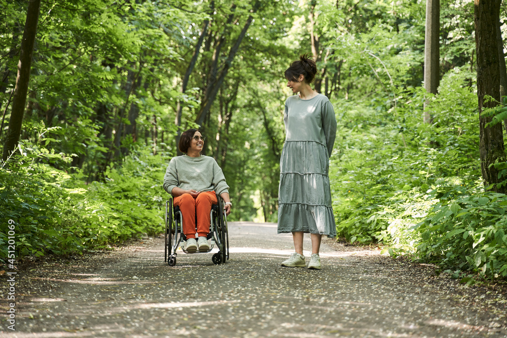 Disabled woman in wheelchair moving herself while walking with her ...