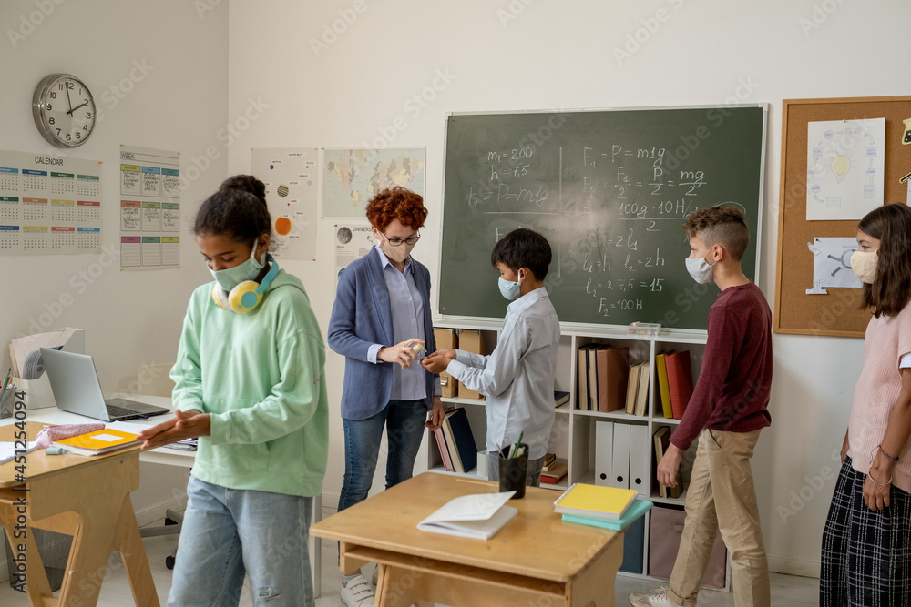 Teacher with sanitizer spraying it on hands of schoolchildren in ...