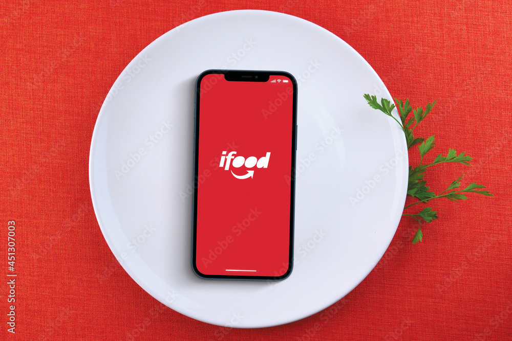 Ifood app on smartphone screen inside an empty white plate. Ifood logo ...